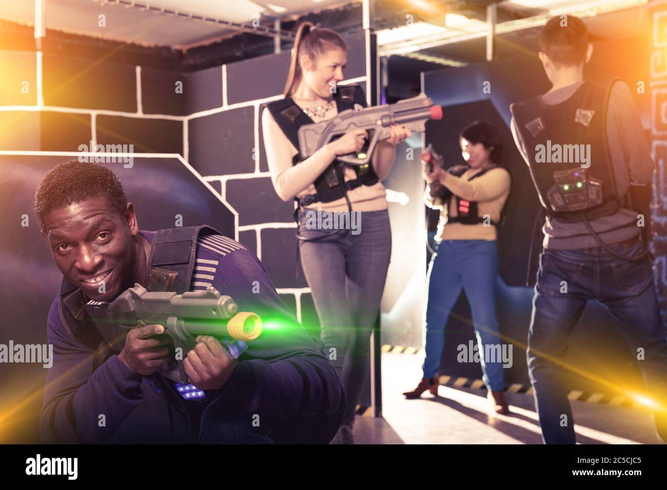 Excited African American man aiming laser pistol at other players ...