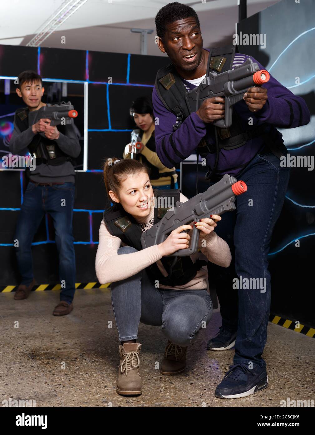 Nice laser tag players of different nationalities aiming laser guns at ...