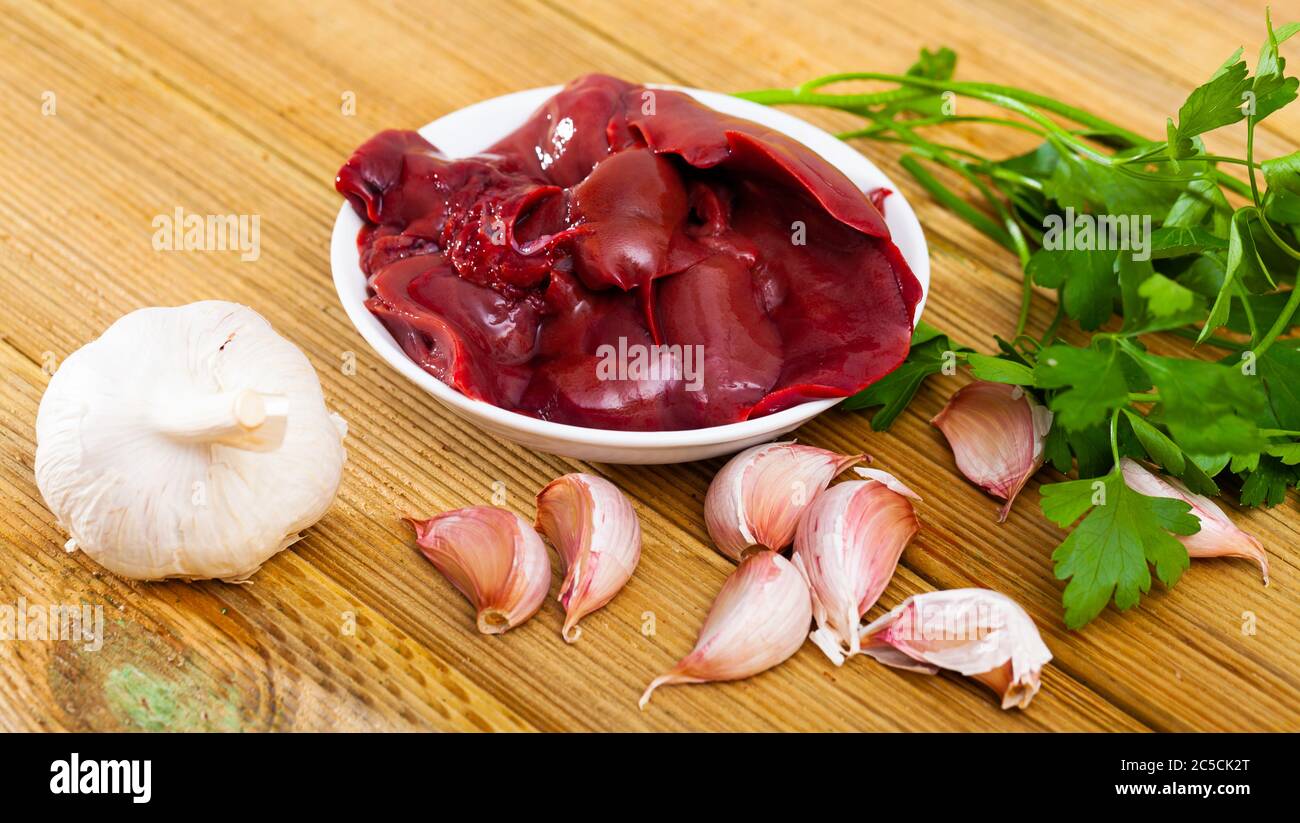 Fresh rabbit liver on wooden background with parsley, garlic and onion ...