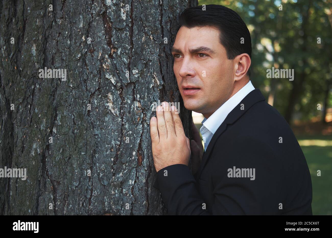 man standing near the tree looking away. Serious guy is looking out ...