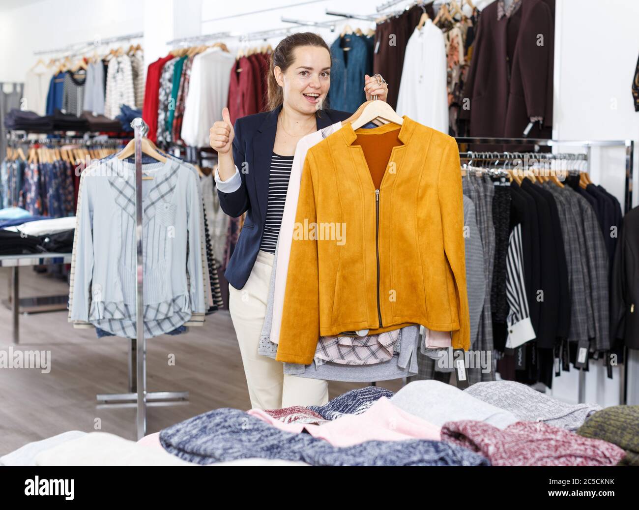 Young cheerful woman demonstrating clothes on hangers in clothing ...