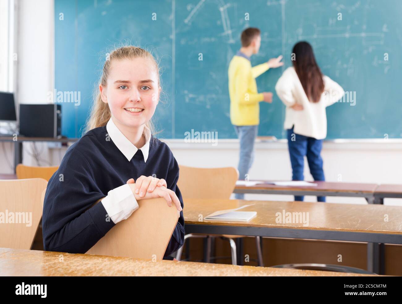 Portrait of girl student in auditorium, students writing on whiteboard ...