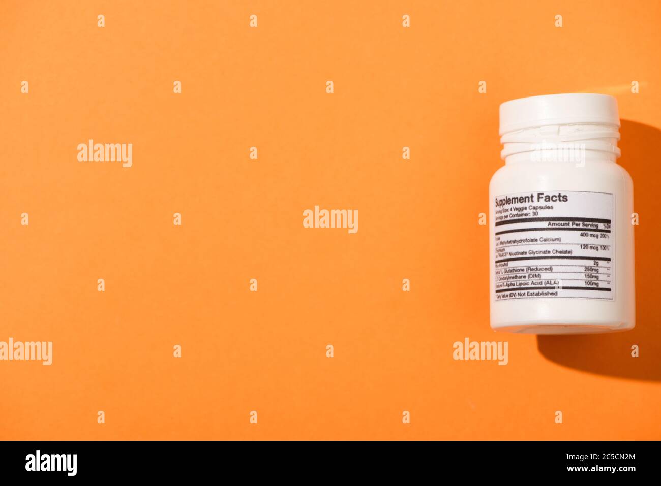 Top view of white container with dietary supplements on orange ...