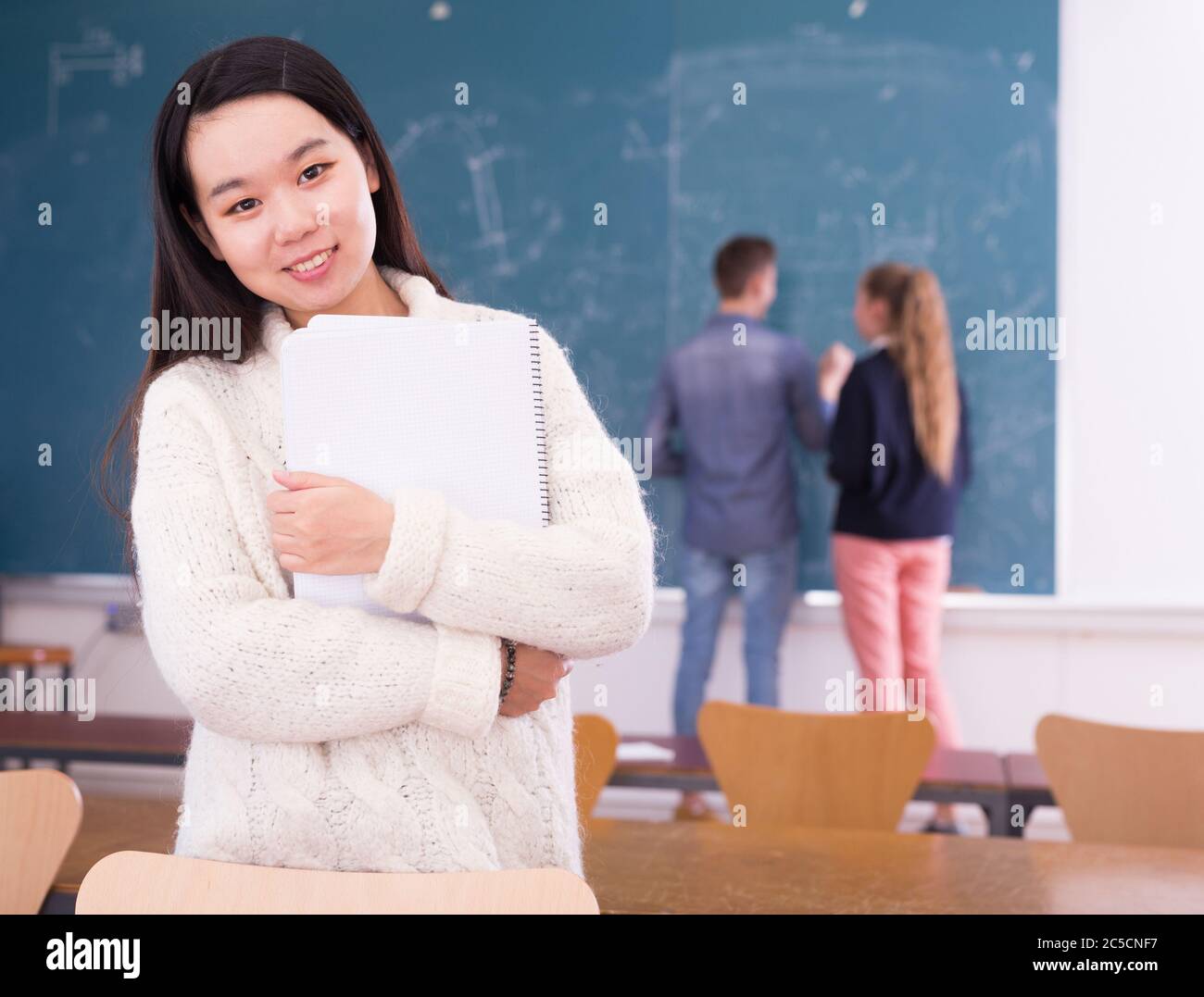 Smiling Chinese teenage girl student standing in classroom with ...