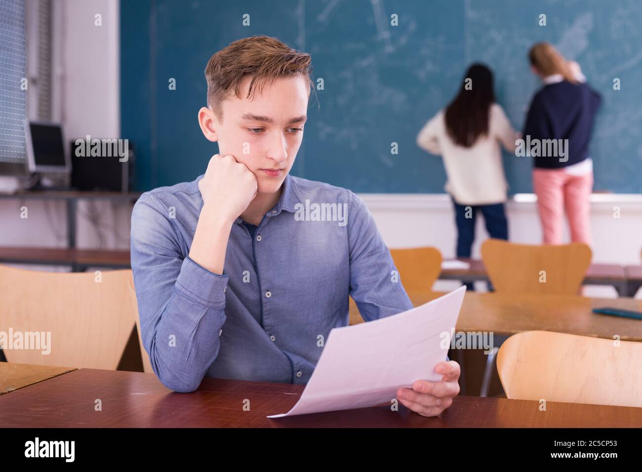 Upset teen student looking at failed exam sitting at desk in schoolroom ...