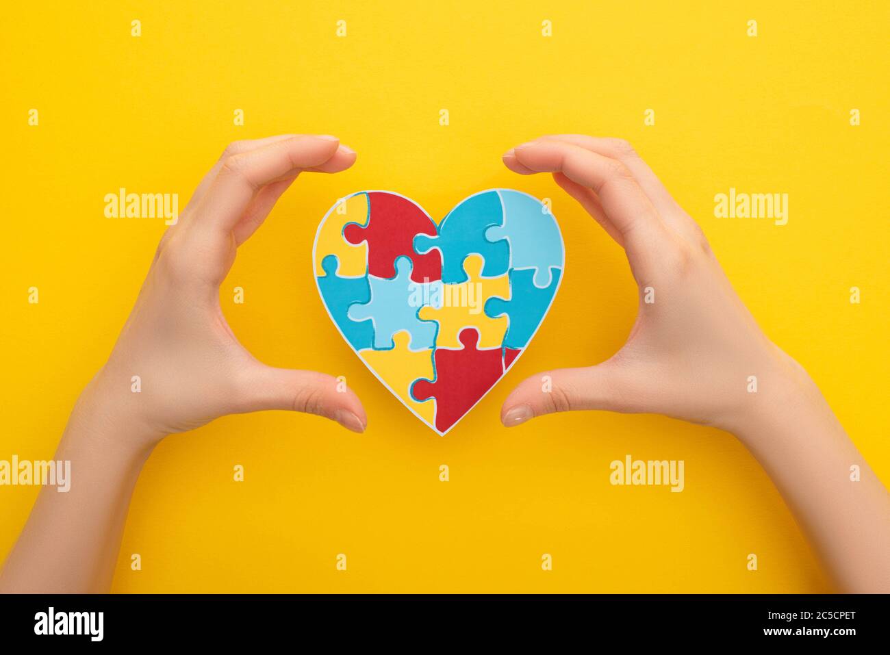 cropped view of female hands with puzzle heart on yellow for World ...