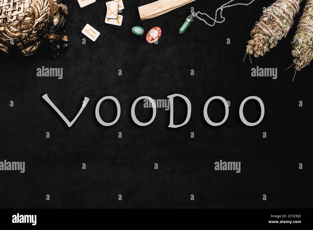 top view of voodoo lettering near runes, amulets and crystals on black ...