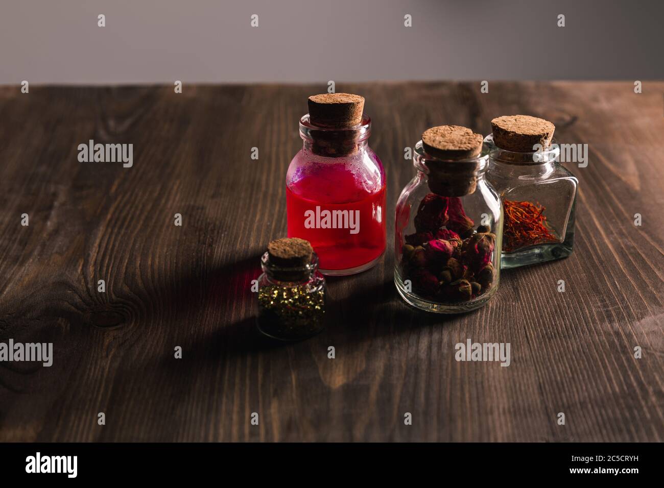 Jars with pink buds, dried herbs and magic tincture on wooden and grey ...