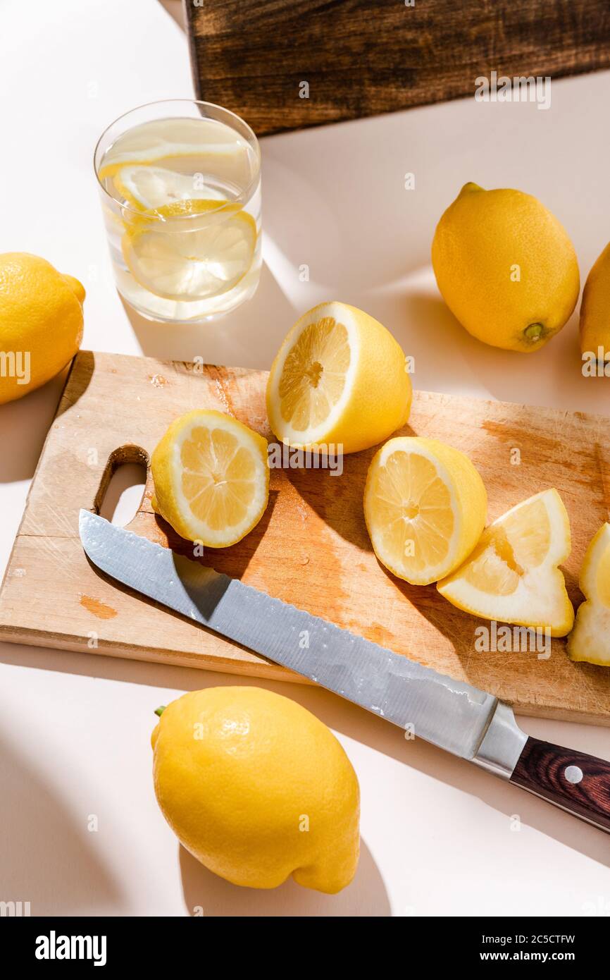 whole and cutted lemons on wooden board with knife and glass of water ...