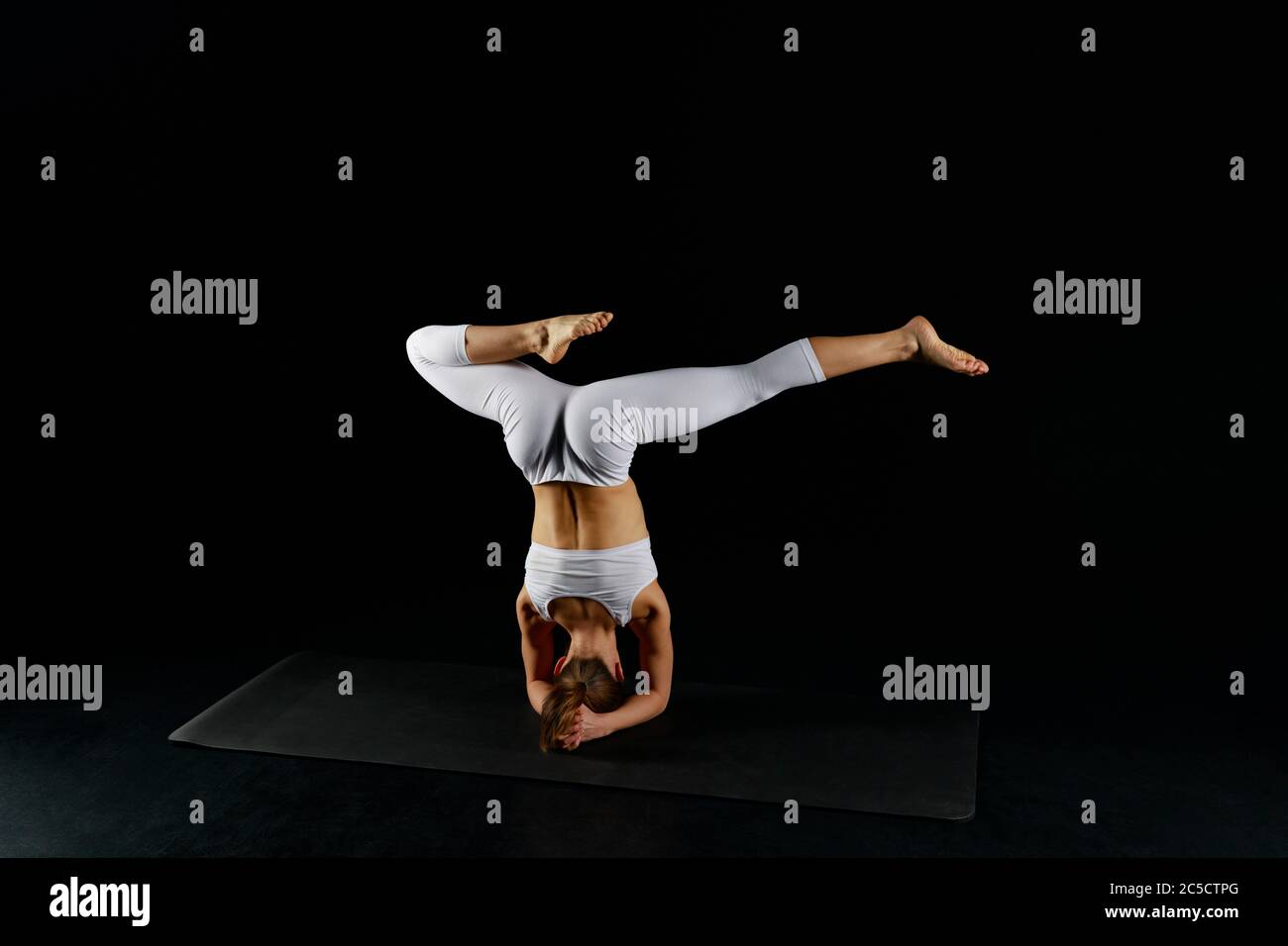 back view of young woman in white sportswear doing handstand isolated ...