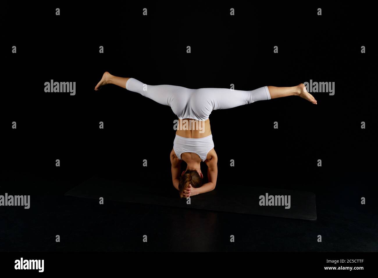 back view of girl in white sportswear doing wide legged headstand ...