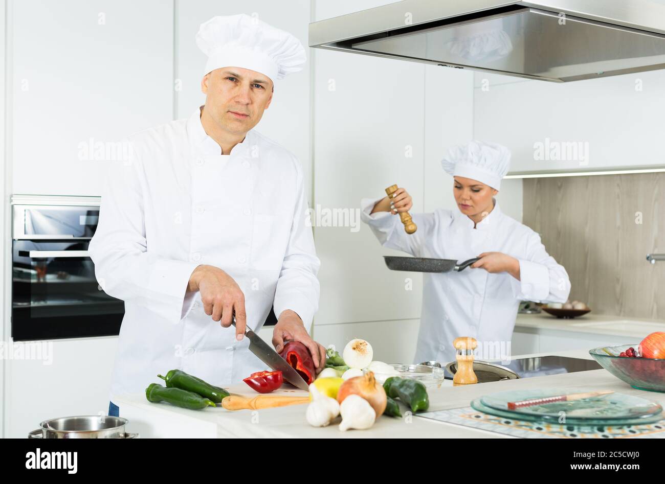 Two positive female and male young cooks wearing uniform working on ...