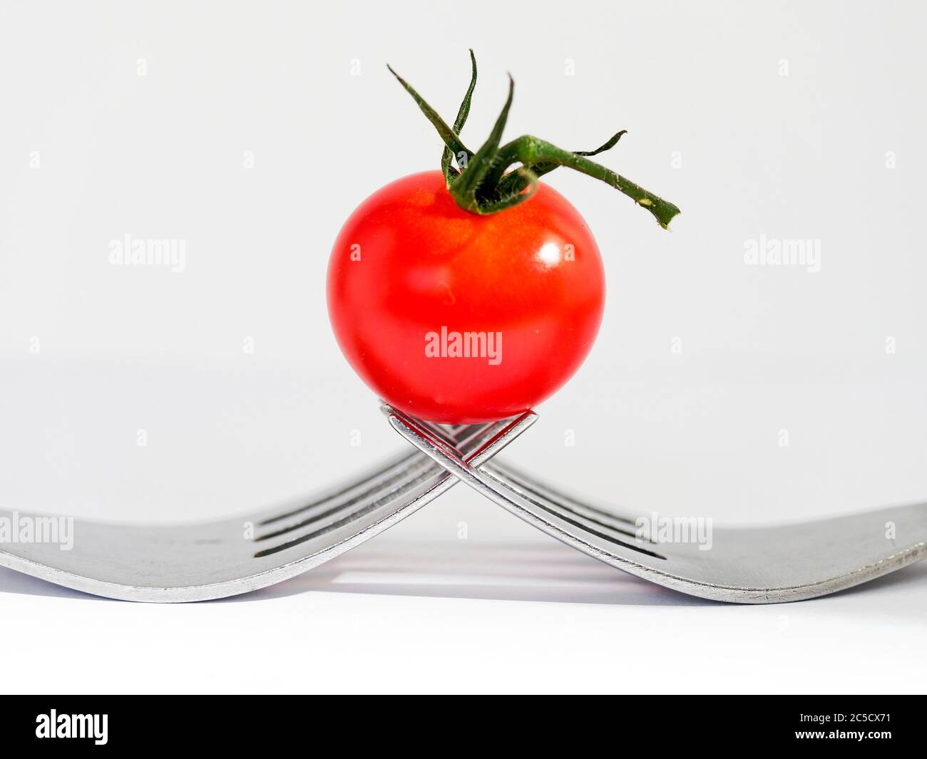 A high-key still life image of a bright red cherry tomato balanced on ...