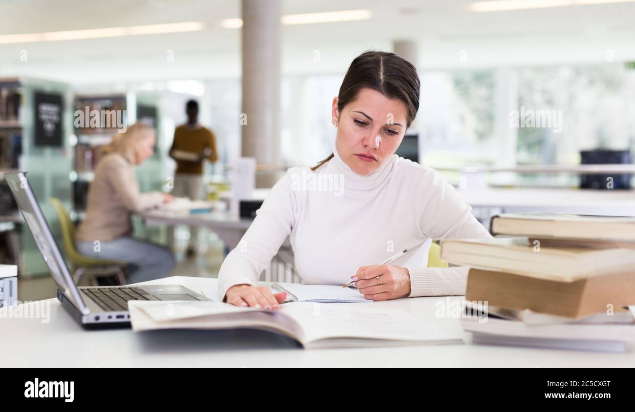 Adult female student with laptop and books in public library Stock ...