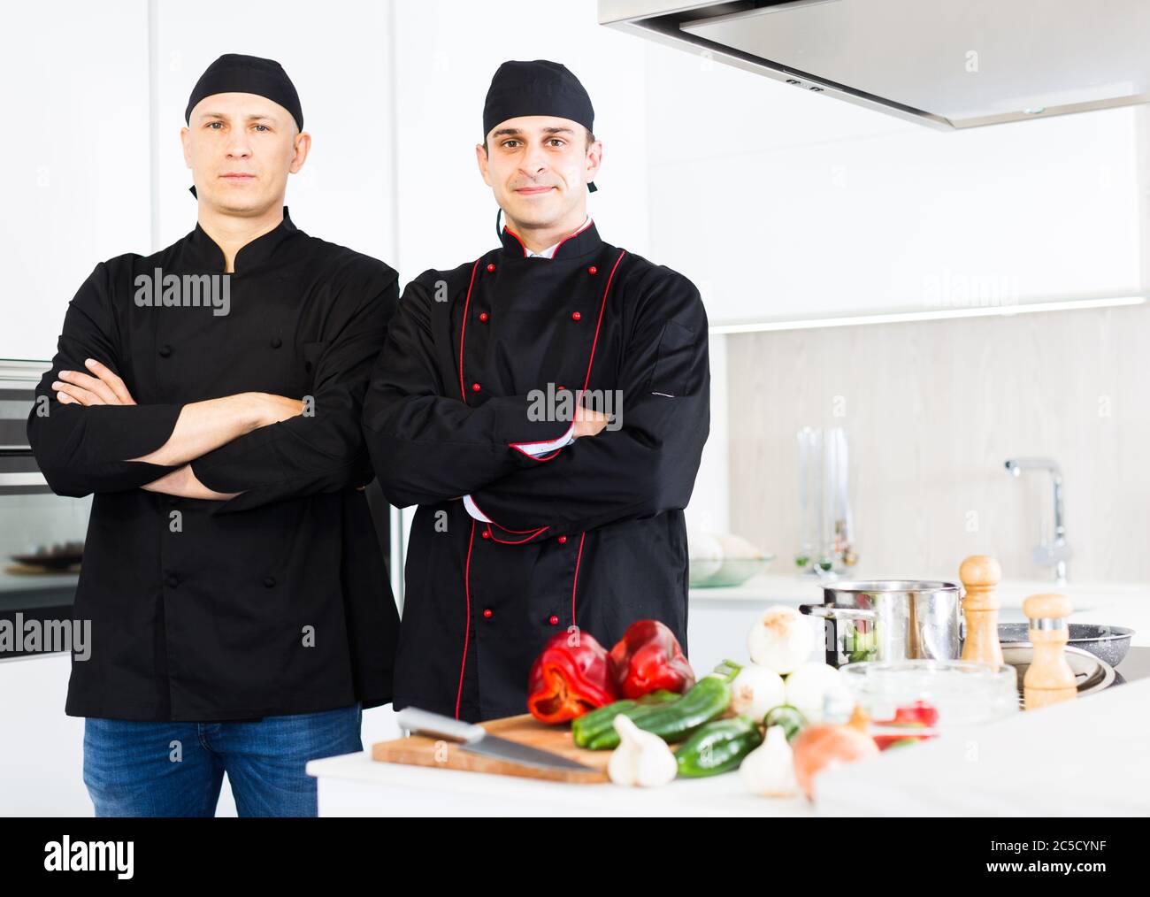 Young male chefs in black uniform standing near workplace on kitchen ...