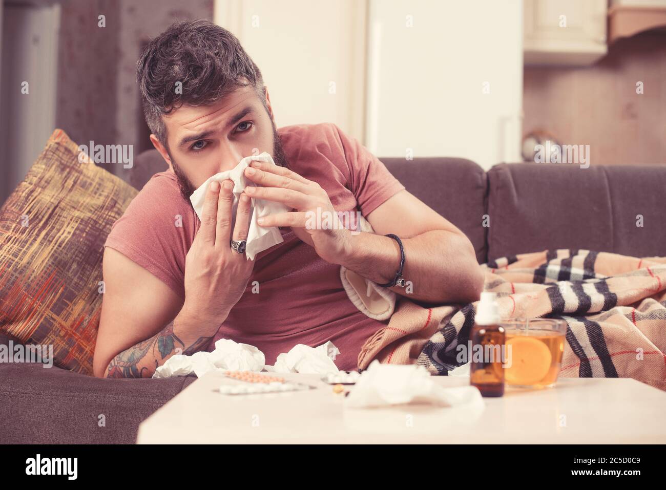Ill young man blowing snot, handkerchiefs are scattered around, wrapped ...