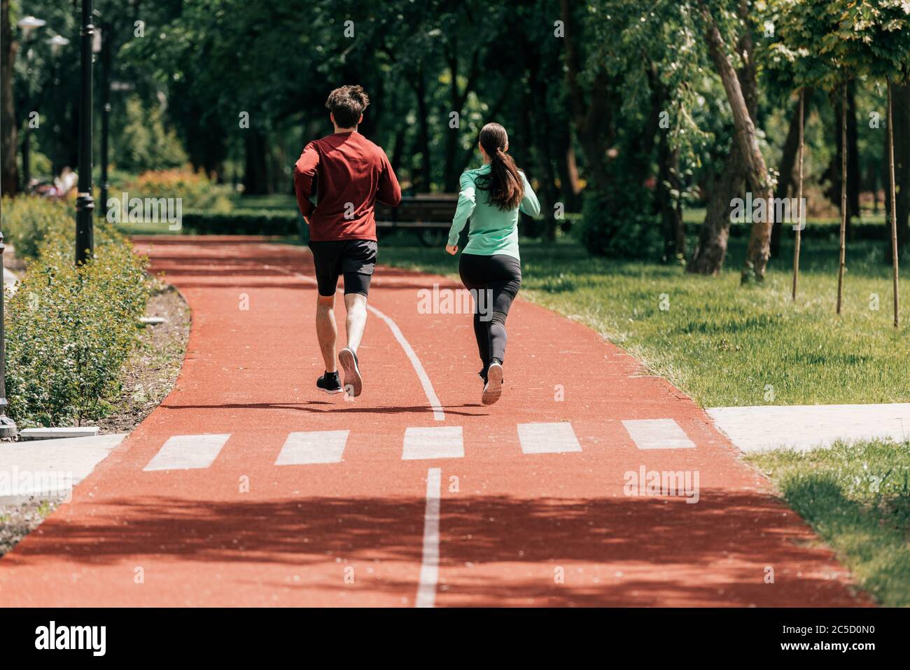 Back view of young couple jogging together on running track in park ...