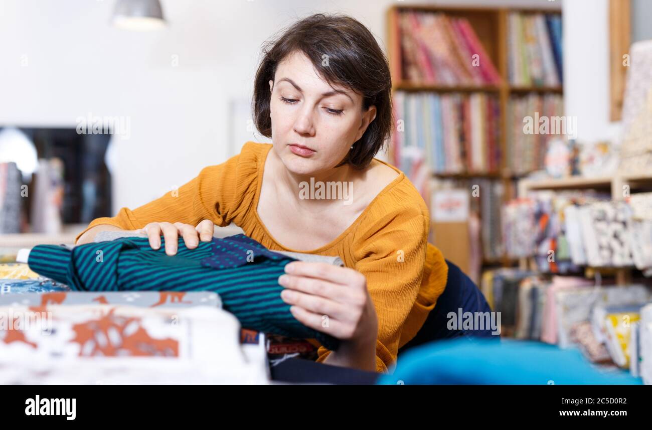 Pensive woman choosing textiles for dressmaking in fabric shop Stock ...