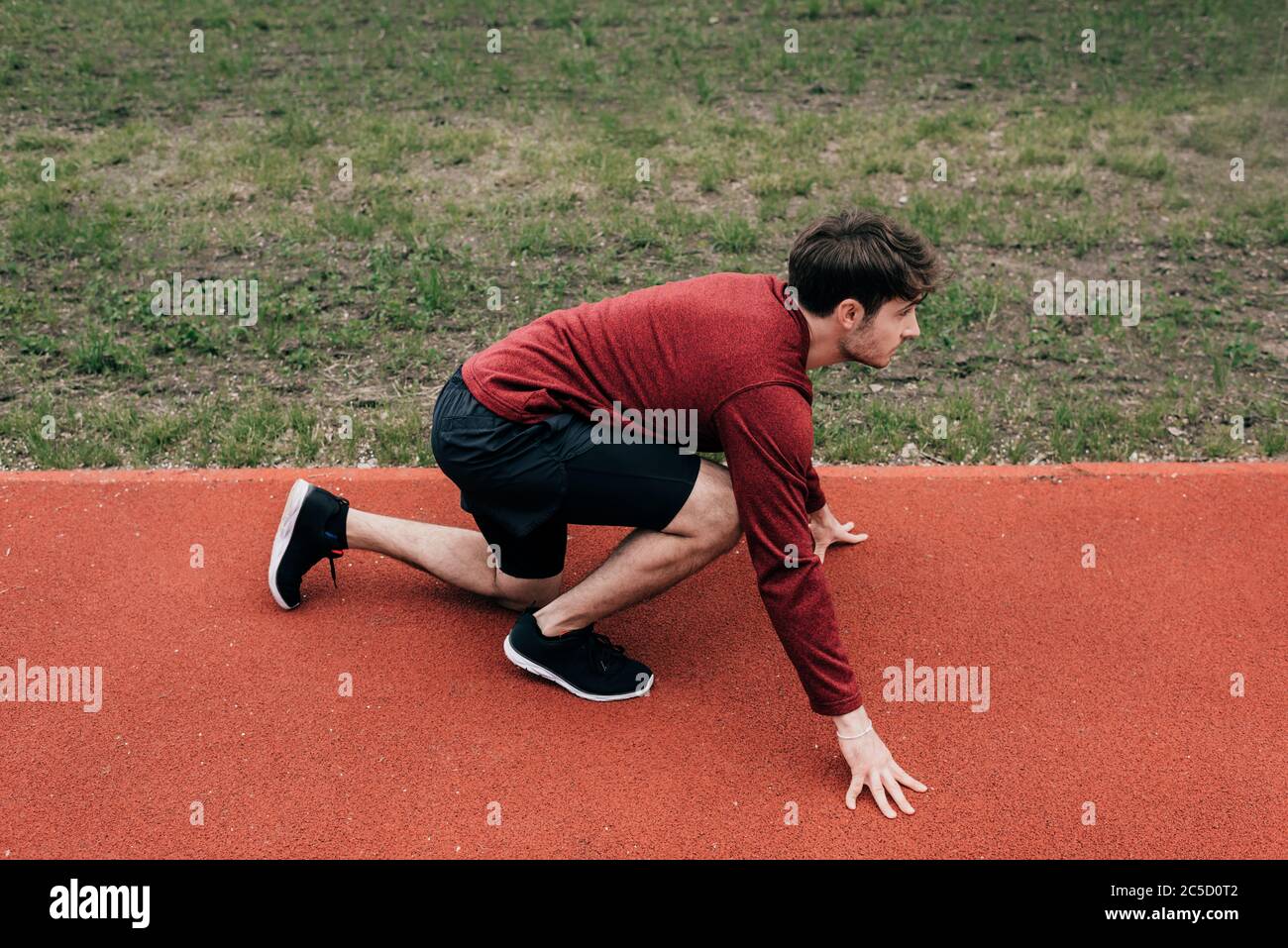 Side view of sportsman in starting position on running track while ...