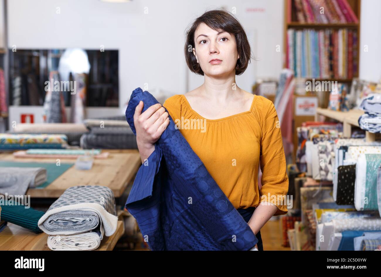 Female seller organizing assortment of textile on shelves in fabric ...