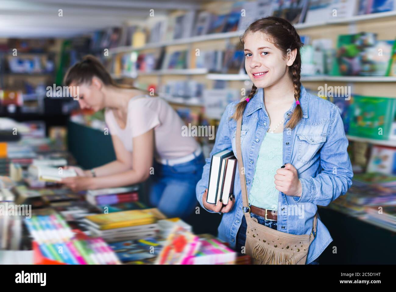 Cheerful girl in school age holding chosen book in hands in bookstore ...