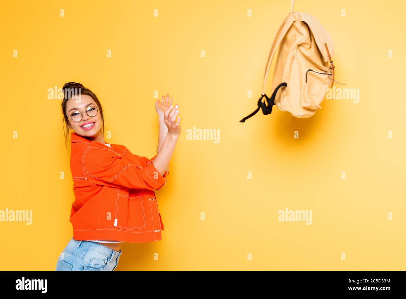 excited student throwing backpack while smiling at camera on yellow ...