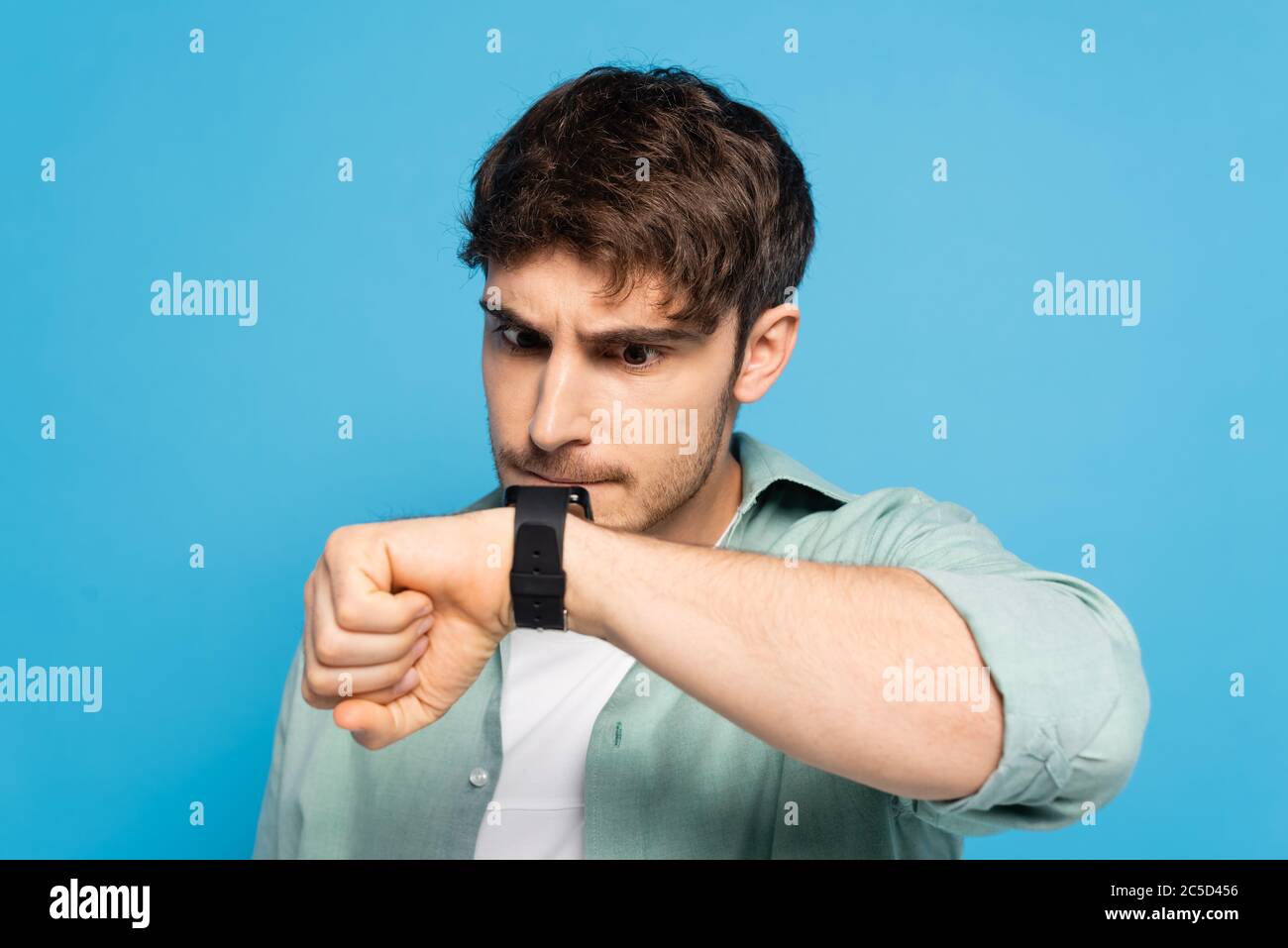 angry young man looking at wristwatch isolated on blue Stock Photo - Alamy
