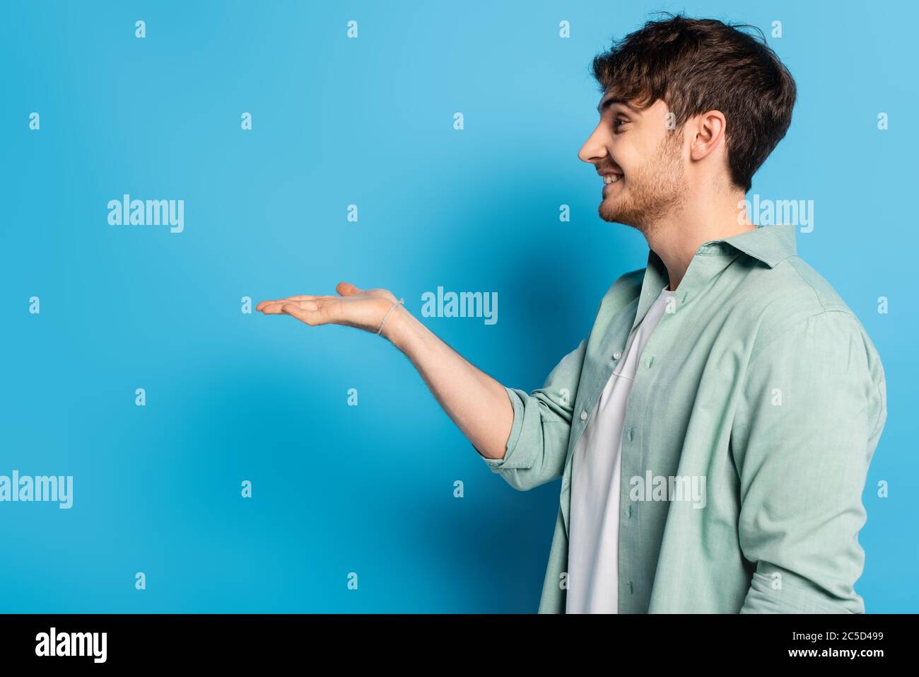 side view of happy young man standing with open arm on blue Stock Photo ...