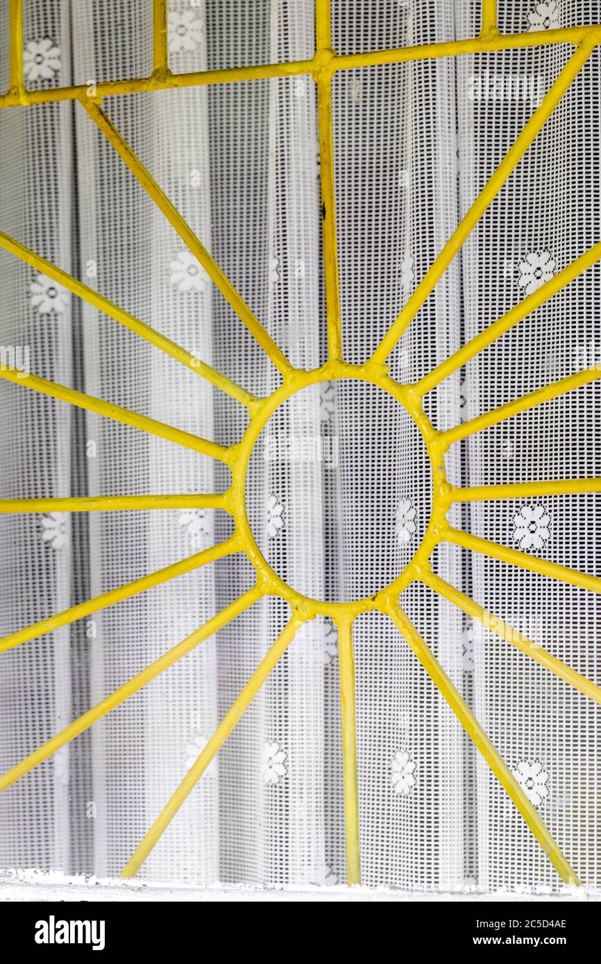 Very old metal yellow window grilles with white curtains background ...