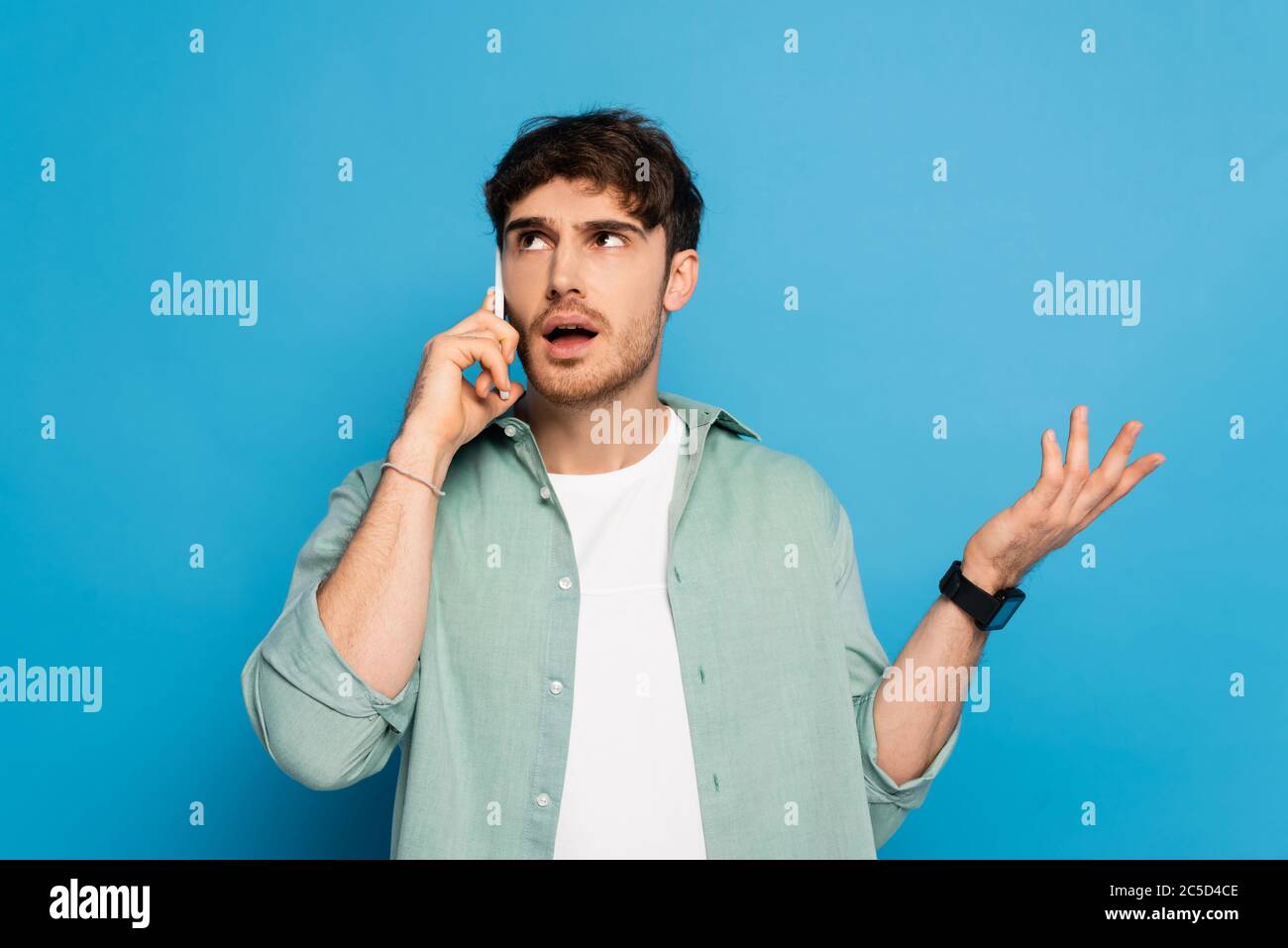 discouraged young man showing shrug gesture while talking on smartphone ...