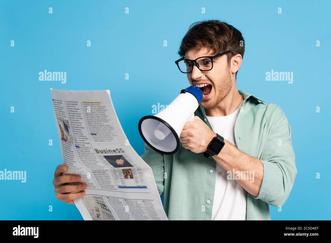 angry young man screaming in megaphone while reading newspaper on blue ...