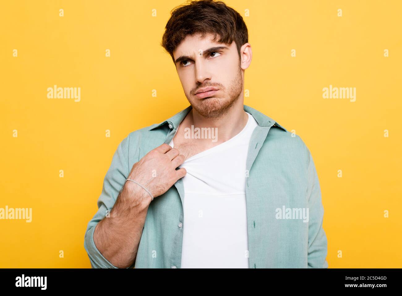 exhausted young man touching shirt while suffering from heat on yellow ...