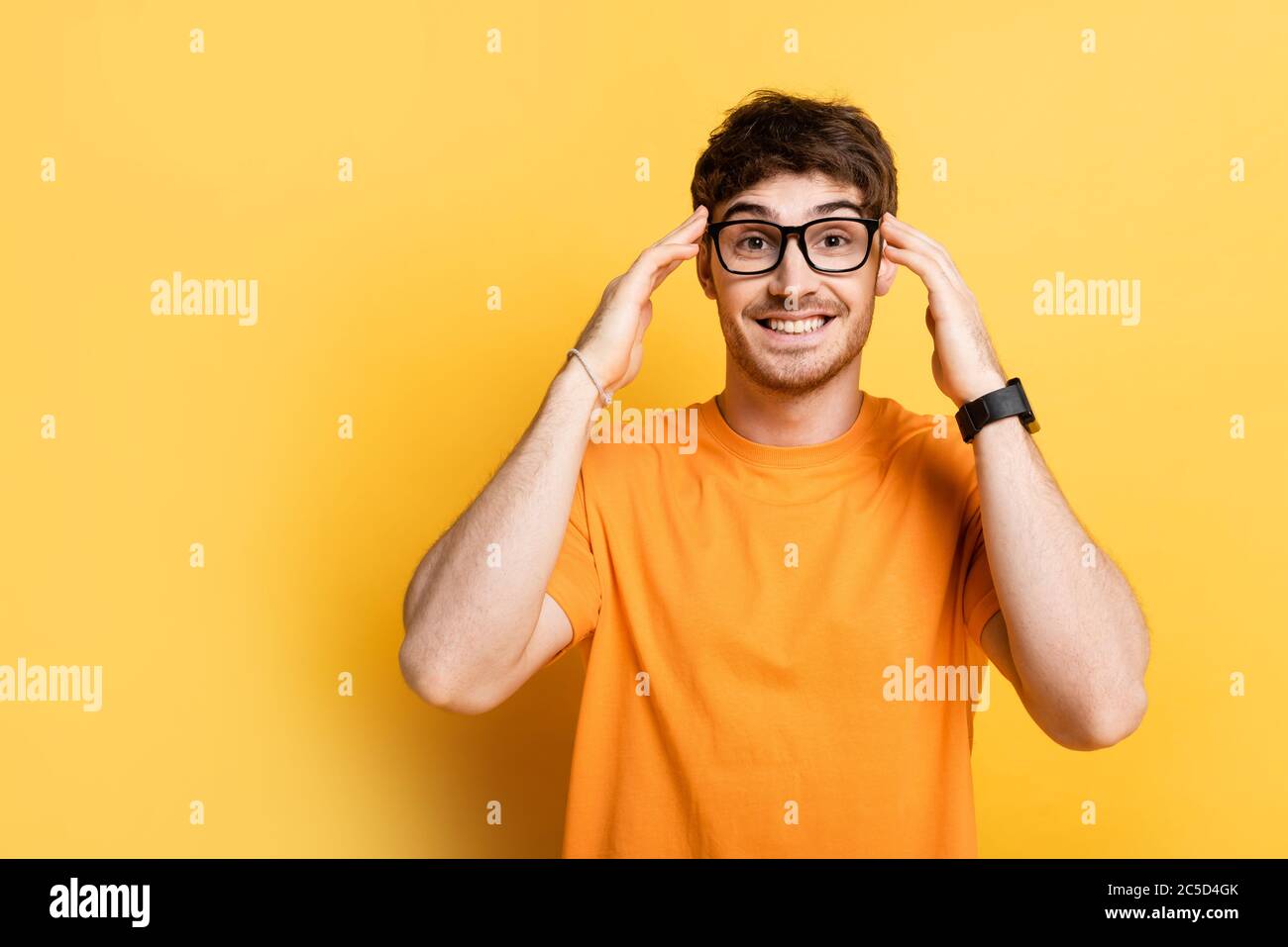 happy young man touching head while looking at camera on yellow Stock ...