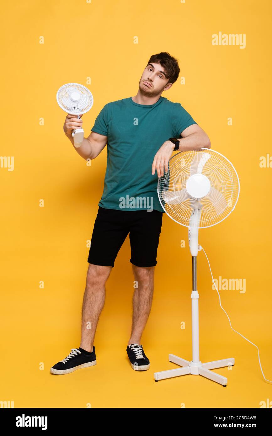 confused man standing with two electric fans on yellow Stock Photo - Alamy