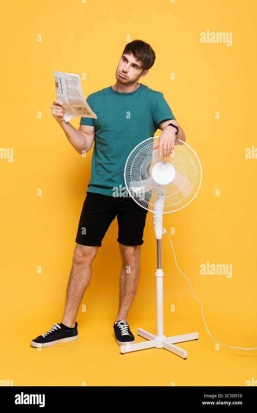 confused man suffering from heat with electric fan and newspaper as ...