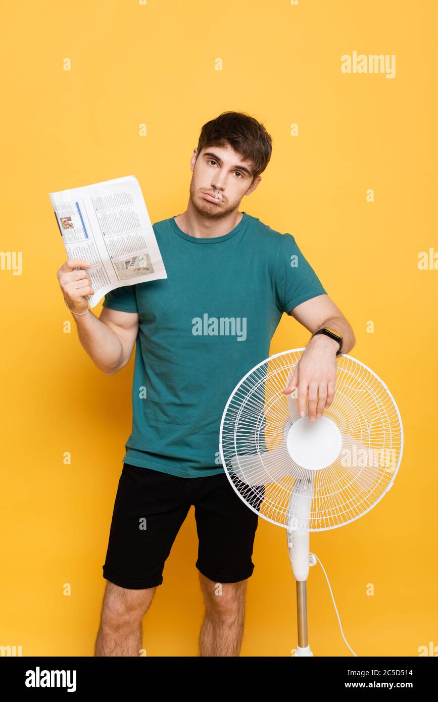sad man suffering from heat with electric fan and newspaper as hand fan ...