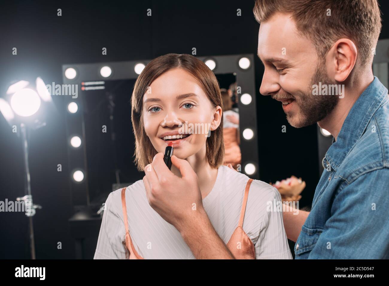 Handsome makeup artist applying red lipstick on beautiful smiling model ...