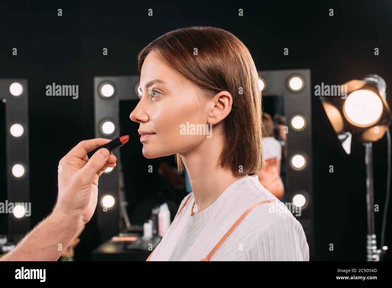 Side view of makeup artist holding red lipstick while doing makeup to ...