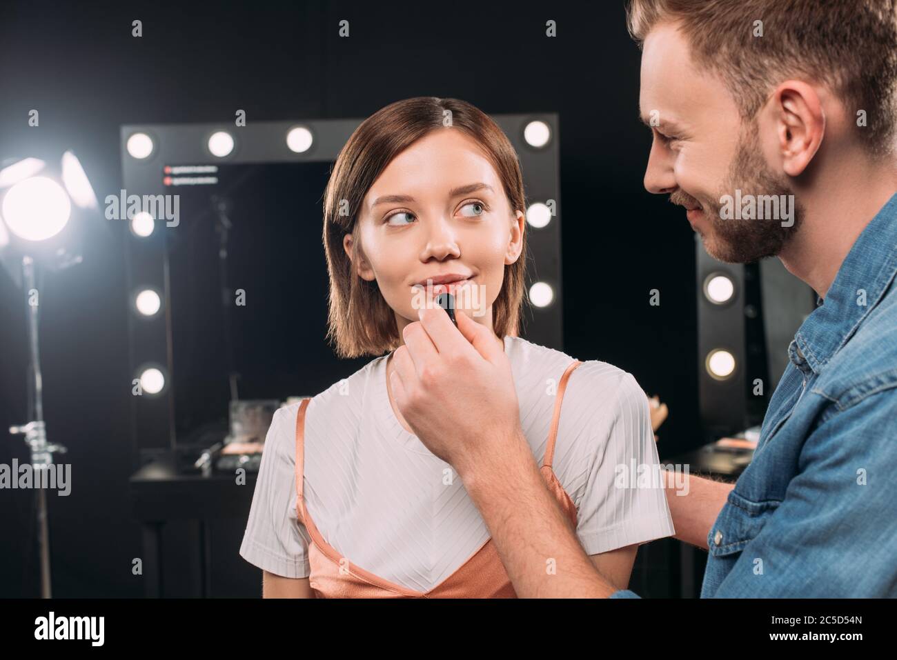 Smiling makeup artist applying red lipstick on attractive young model ...