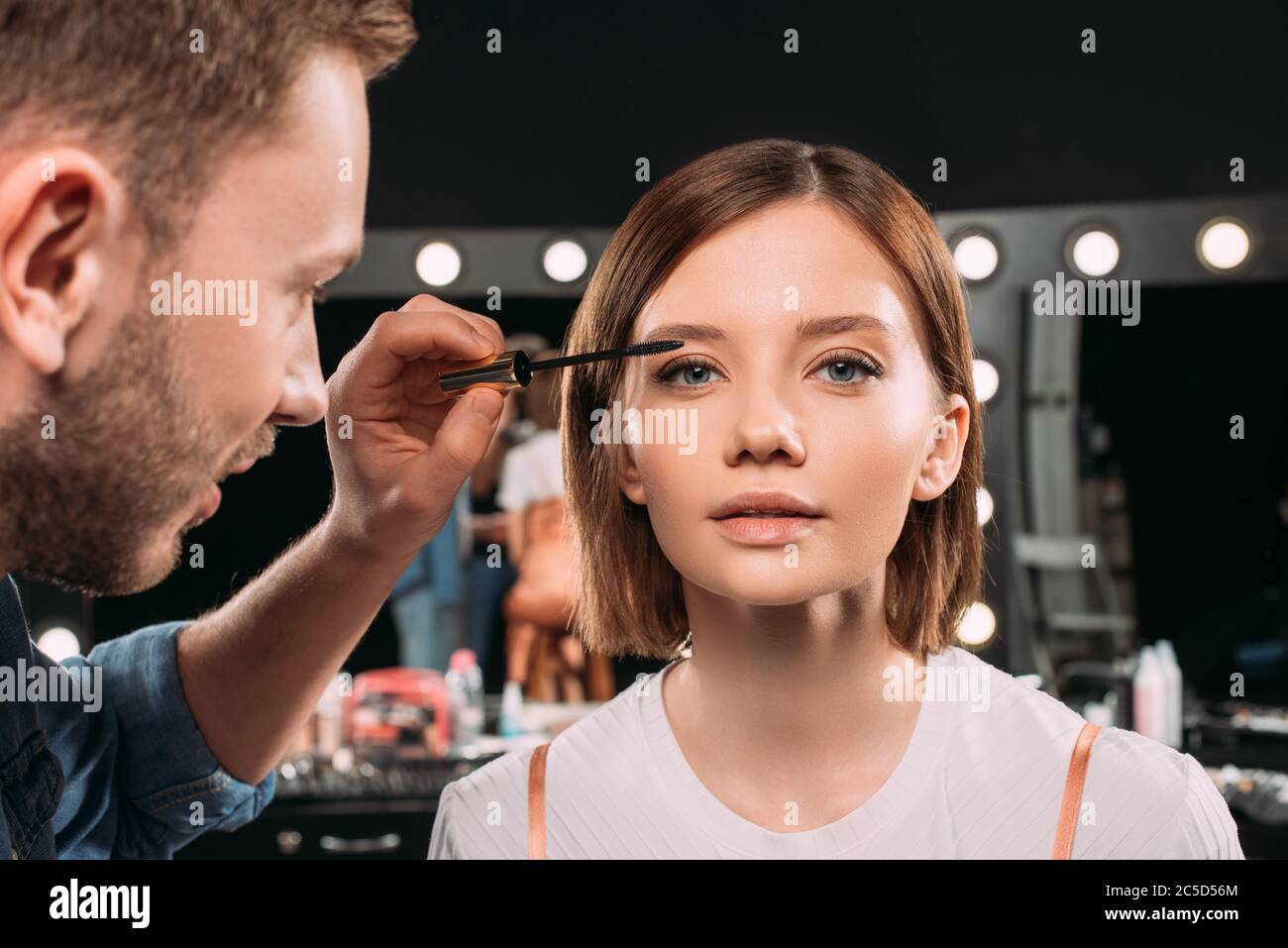 Selective focus of makeup artist applying mascara on young model in ...