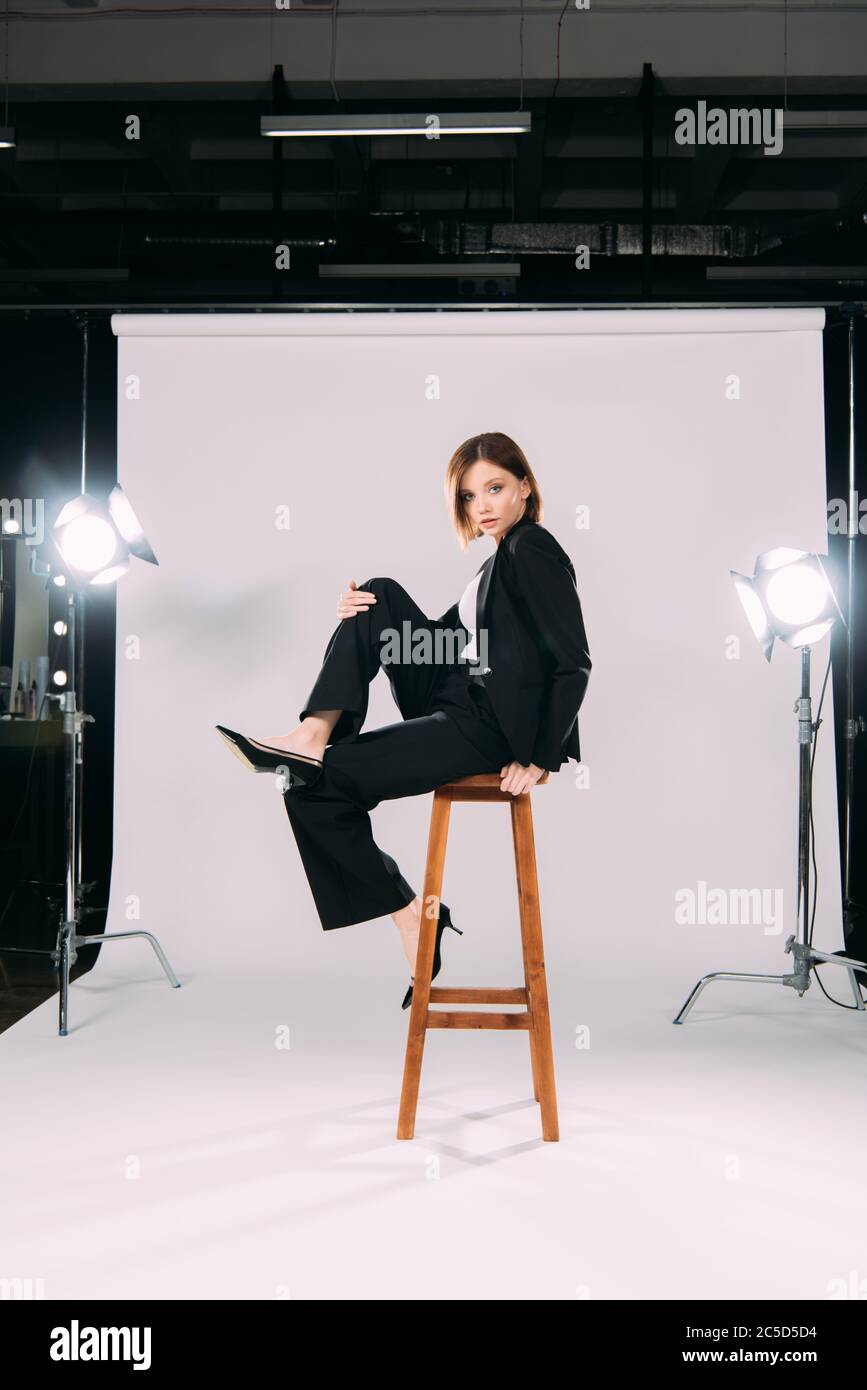 Side view of fashionable model posing on chair in photo studio Stock ...