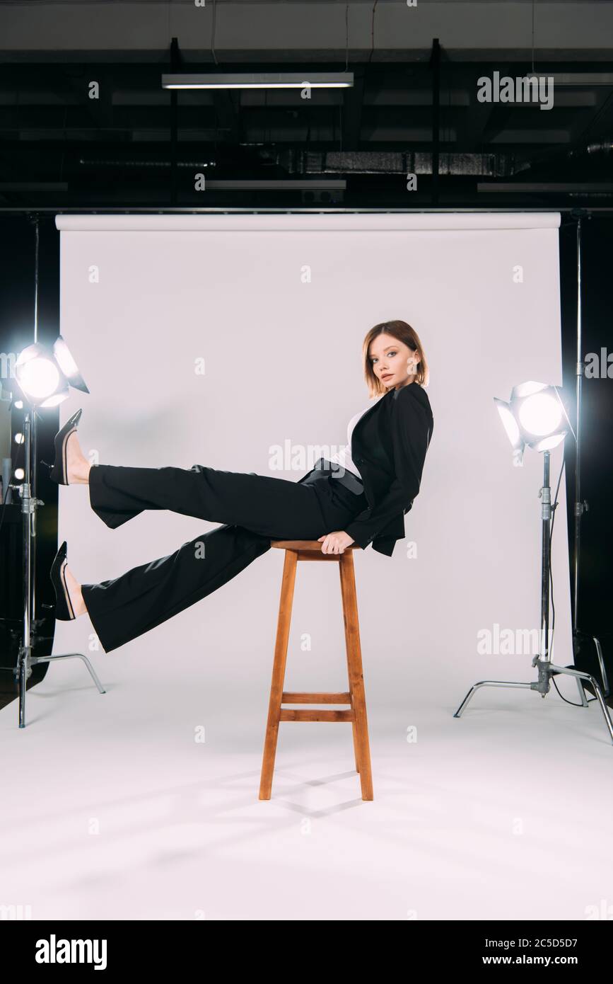 Side view of stylish model looking at camera while sitting on chair in ...