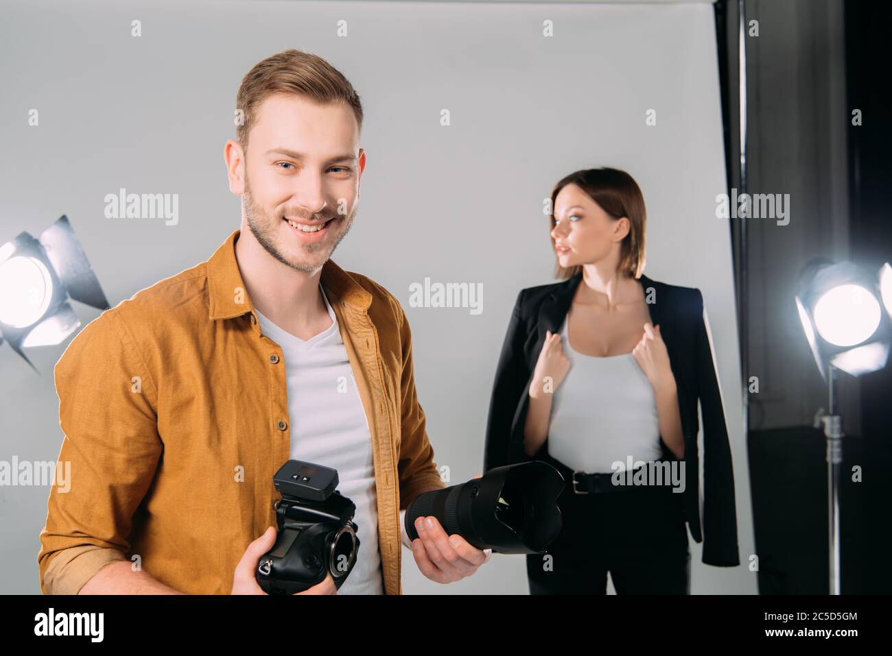 Selective focus of handsome photographer smiling while holding lens and ...