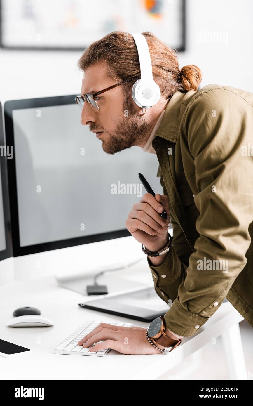 Side view of handsome digital designer in headphones using computer and ...