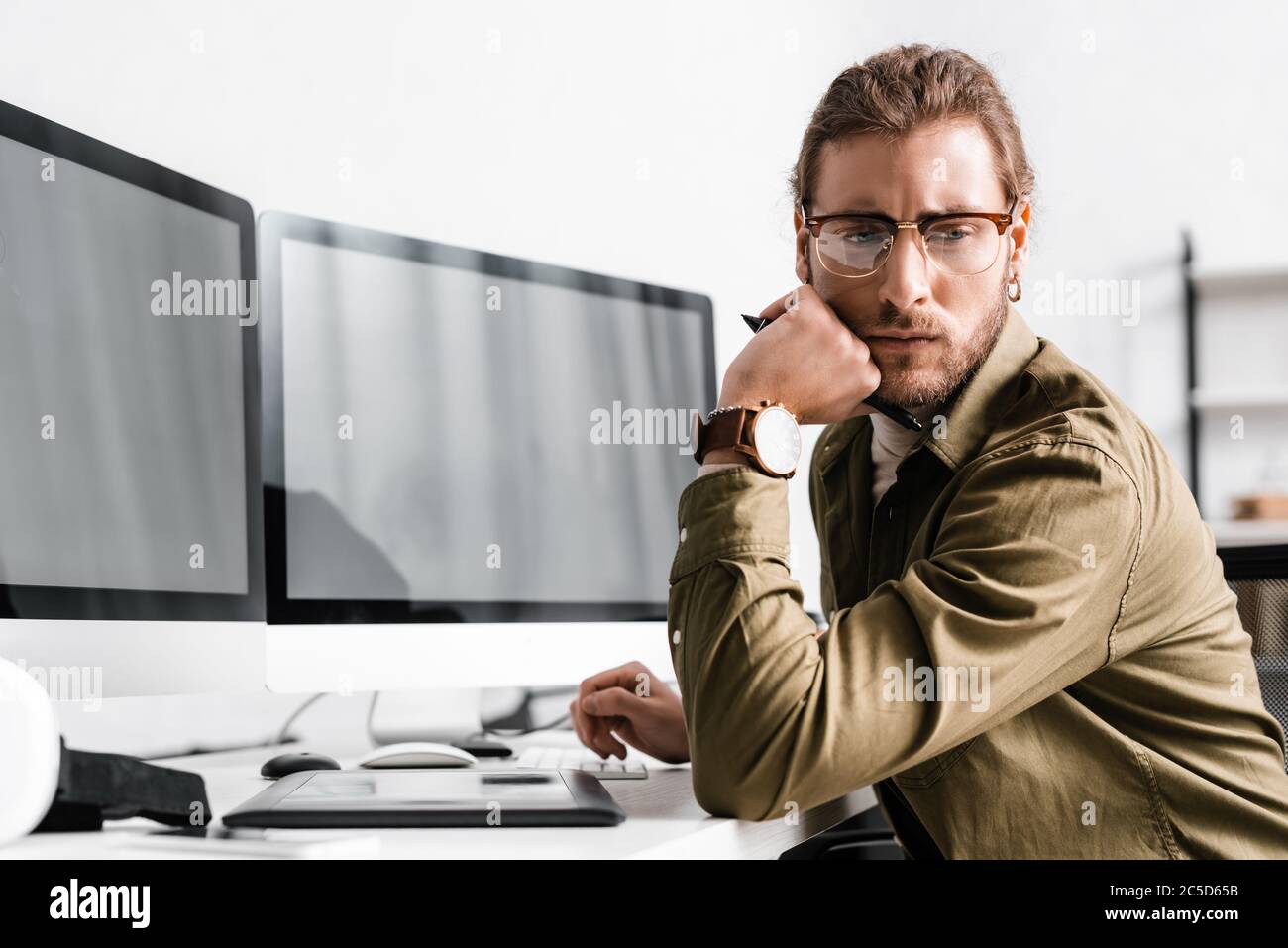 Pensive digital designer looking away near graphics tablet and ...