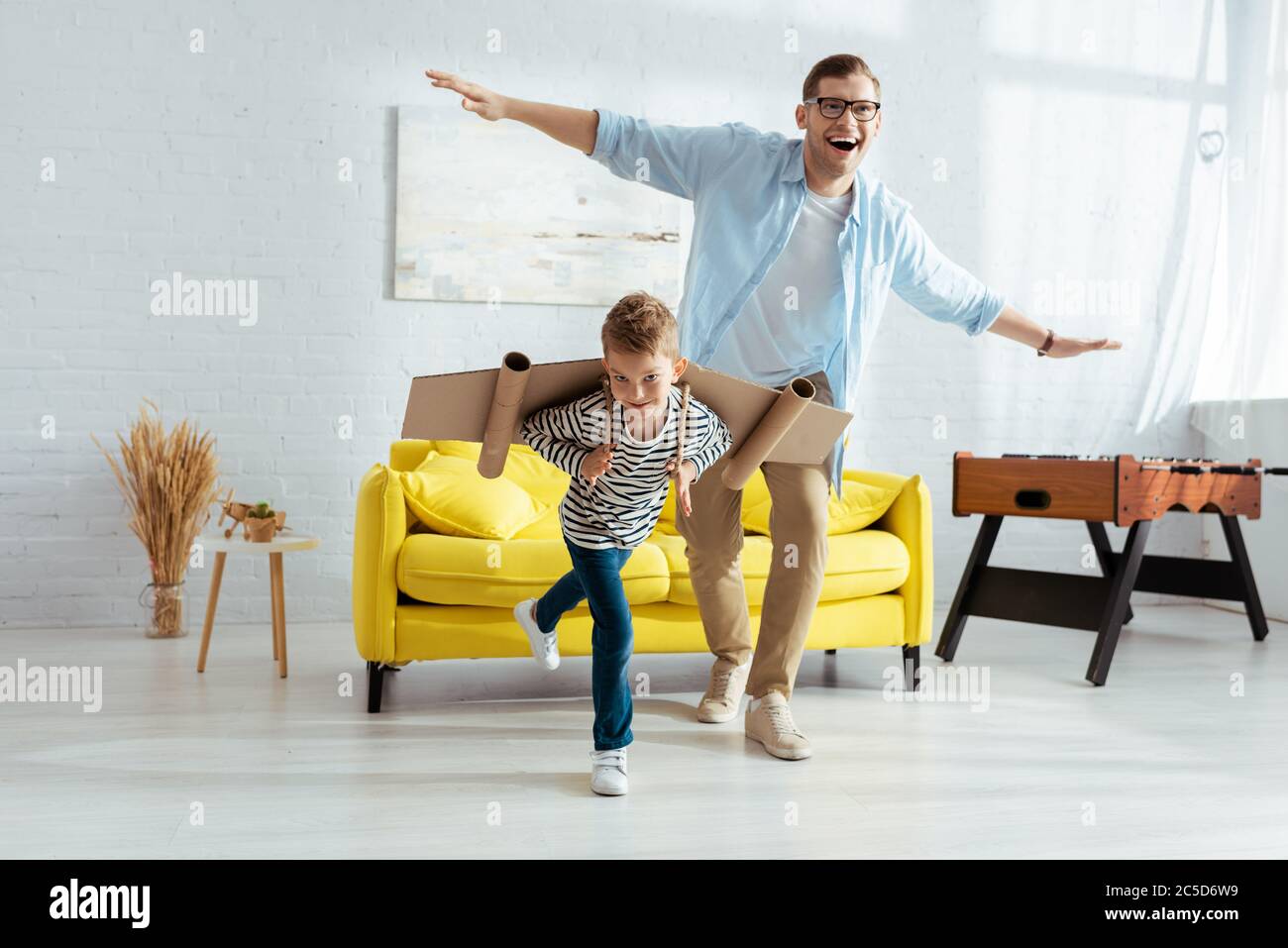 happy boy with carton plane wings, and cheerful father having fun while ...
