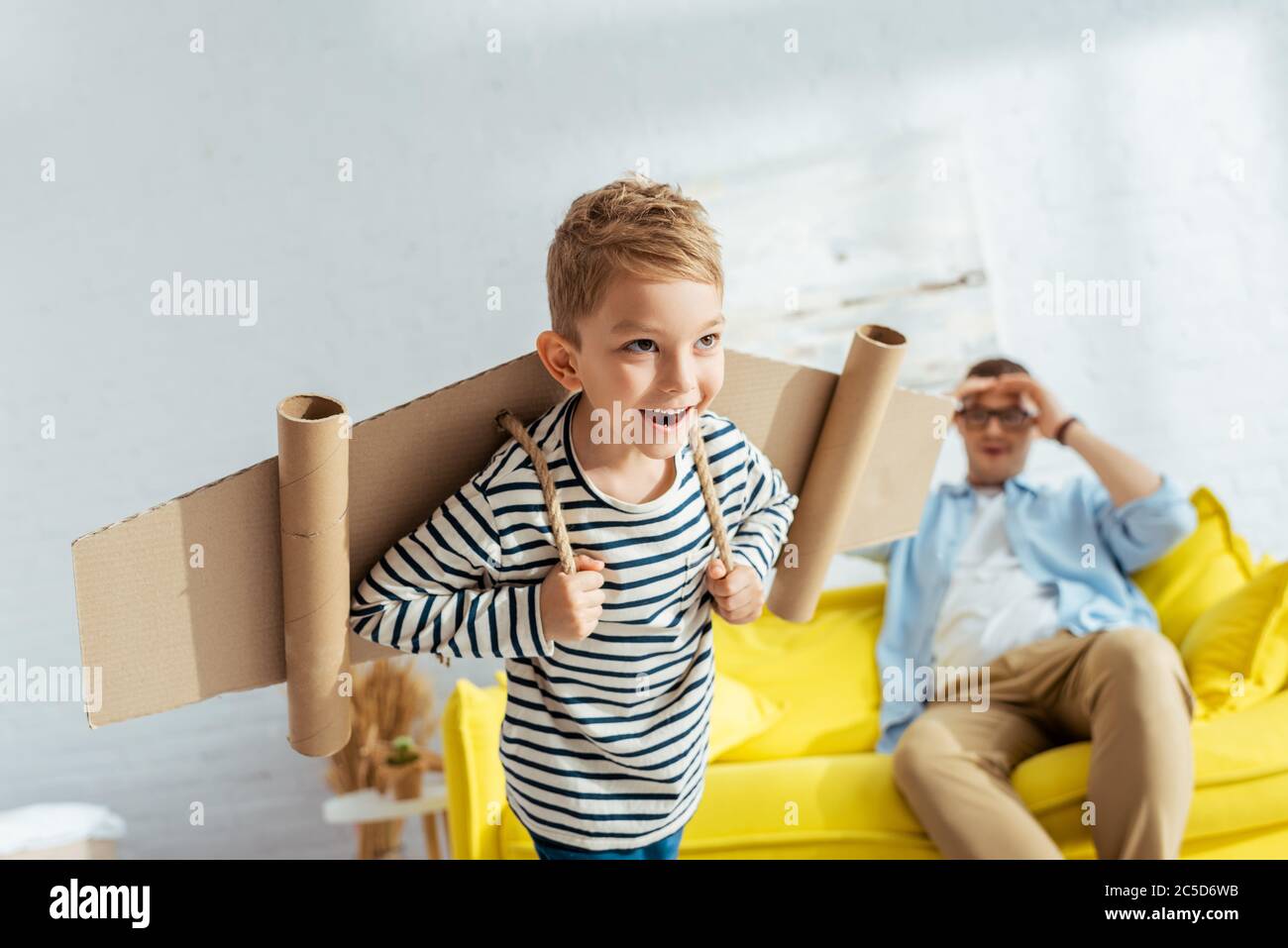 selective focus of happy boy with carton plane wings on back imitating ...