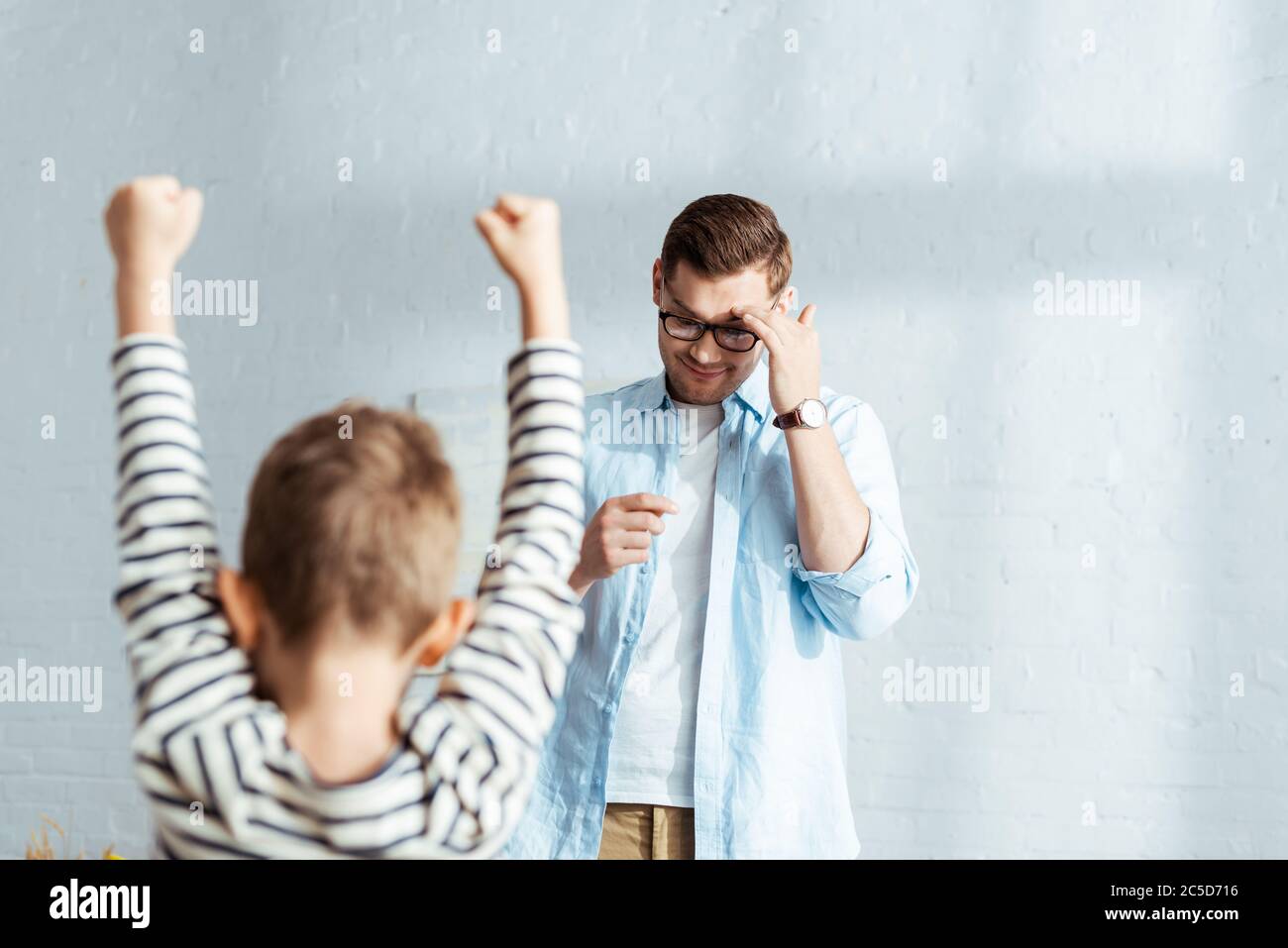 back view of boy showing winner gesture near father touching forehead ...