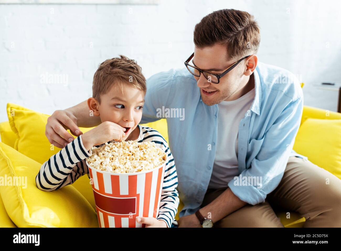 happy father looking at son eating popcorn from bucket Stock Photo - Alamy