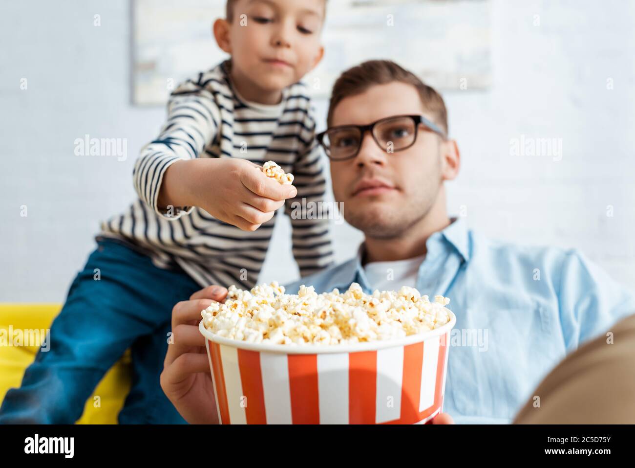 selective focus of cute boy taking popcorn from bucket while ...